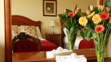 Quarto de hotel com cama de madeira, mesa de cabeceira, espelho e um vaso com flores.