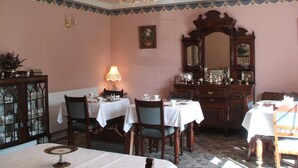 Uma sala de jantar com um candelabro, um espelho grande e uma mesa posta para quatro pessoas.