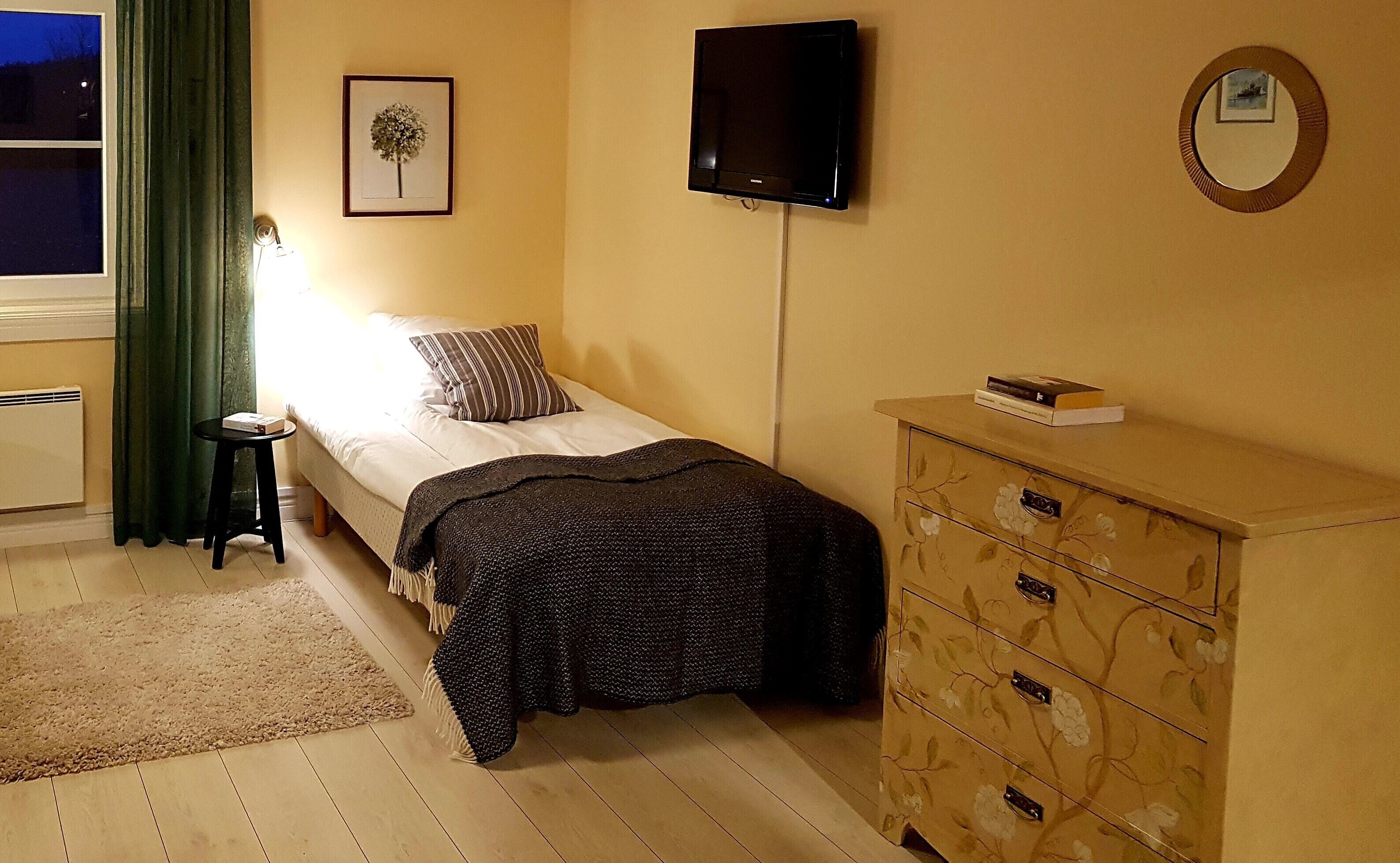 Quarto com cama, cômoda, televisão e um quadro na parede.