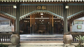 Entrada de um edifício tradicional com chão de azulejos, uma mesa central e dois vasos grandes.