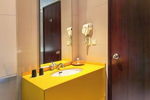 Casa de banho com lavatório amarelo, espelho, secador de cabelo e porta.