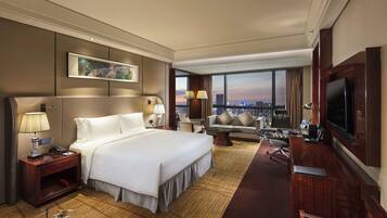 Quarto de hotel com uma cama grande, uma escrivaninha, televisão e vista para a cidade.