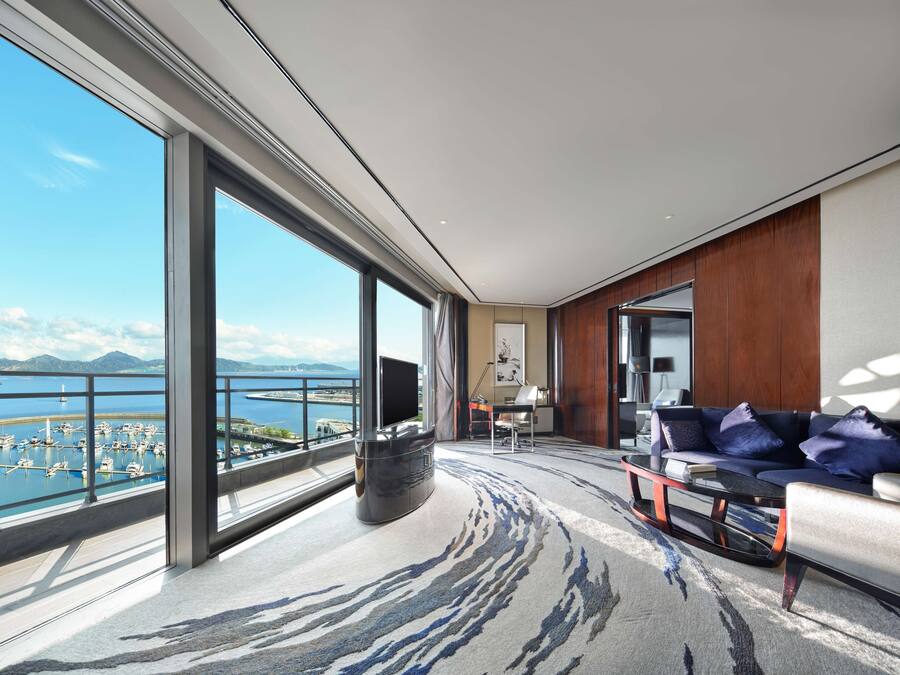 Quarto de hotel moderno com uma varanda grande, um sofá, uma mesa de centro e uma televisão.