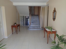 Um corredor com escada que dá para um patamar. Há duas mesas laterais de madeira, com plantas, e um espelho na parede.
