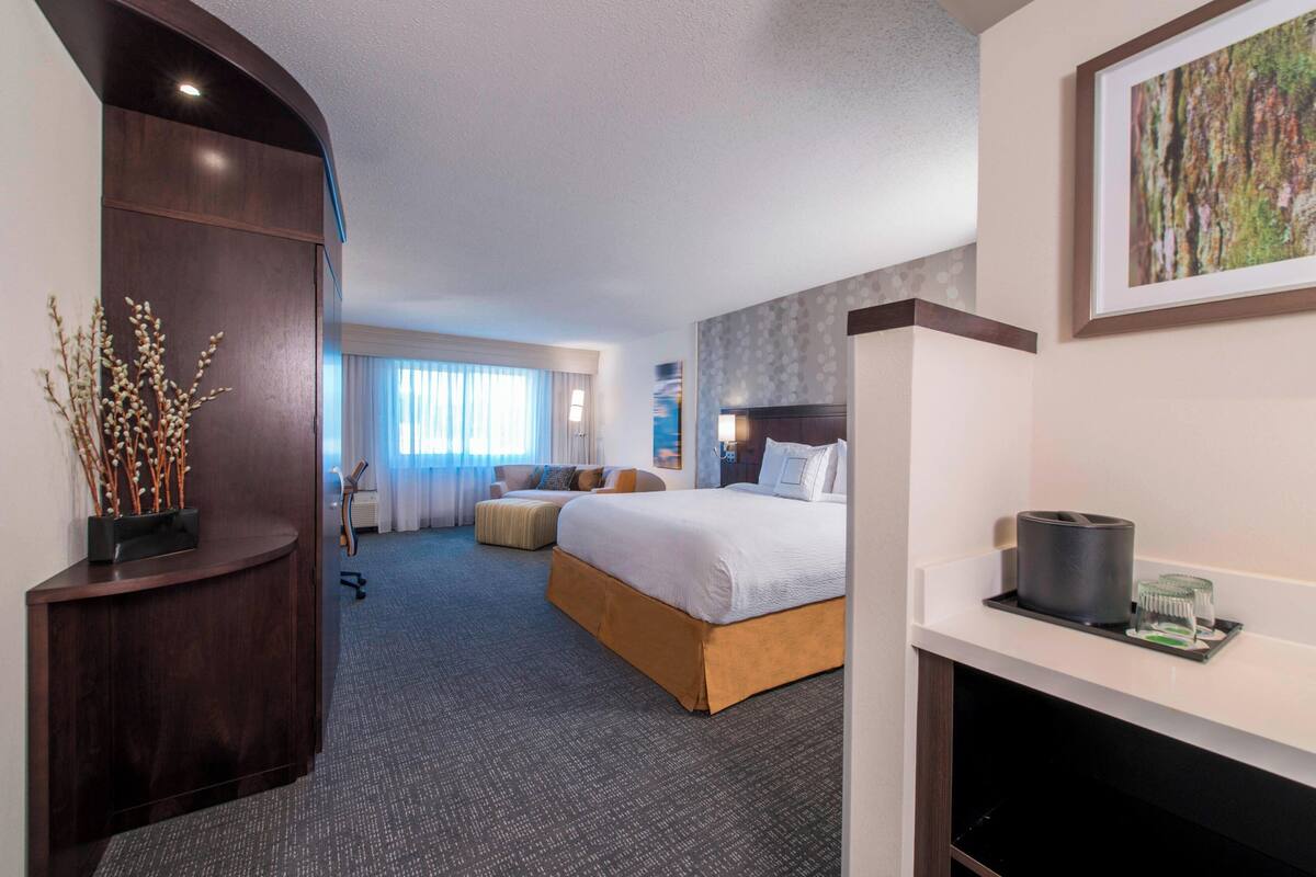 Quarto de hotel com uma cama grande, uma escrivaninha, uma cadeira e uma pequena mesa com uma chávena e uma caixa de lenços.