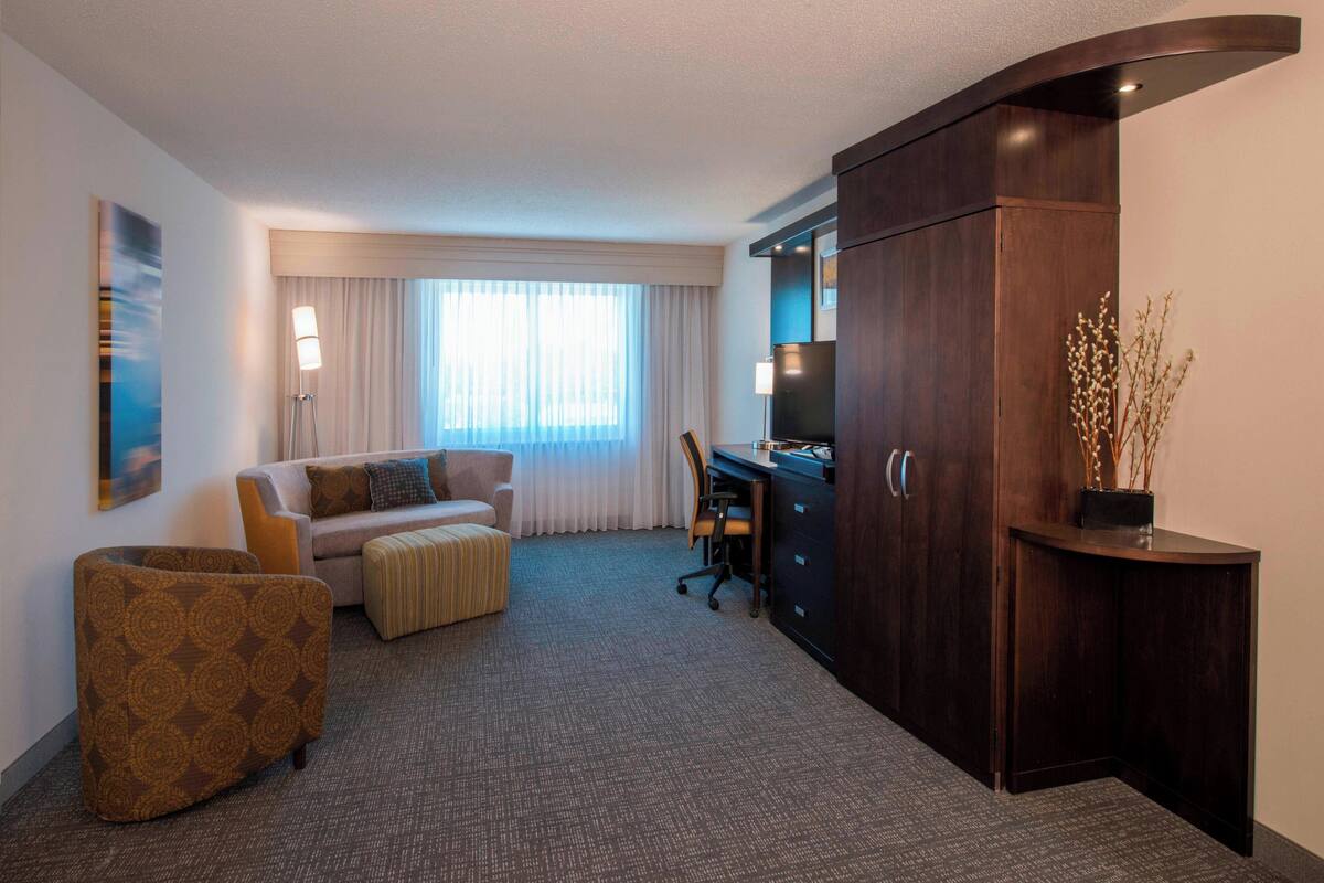 Quarto de hotel com sofá, poltrona, escrivaninha e guarda-roupa.