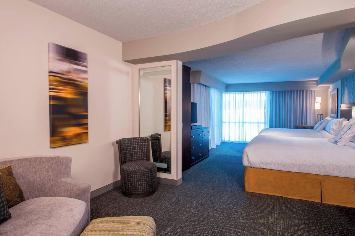 Quarto de hotel com uma cama, um sofá, uma poltrona, uma mesinha e um quadro na parede.