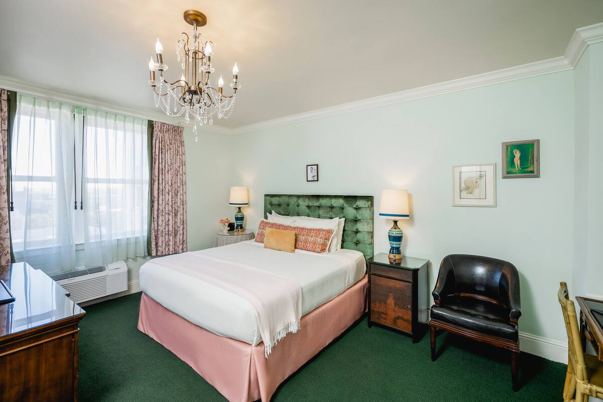 Quarto de hotel com uma cama grande, um candelabro, uma escrivaninha e uma cadeira.