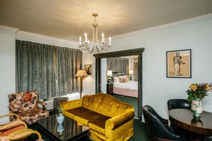 Quarto de hotel com sofá amarelo, mesa de jantar, espelho e lustre.