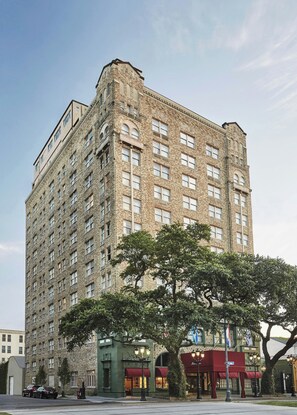 Um edifício de vários andares com fachada de pedra, grandes janelas e uma árvore na frente.