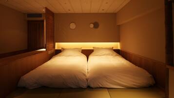 Uma cama de casal com cabeceira de madeira e mesa de cabeceira, em quarto com teto inclinado e iluminação embutida.