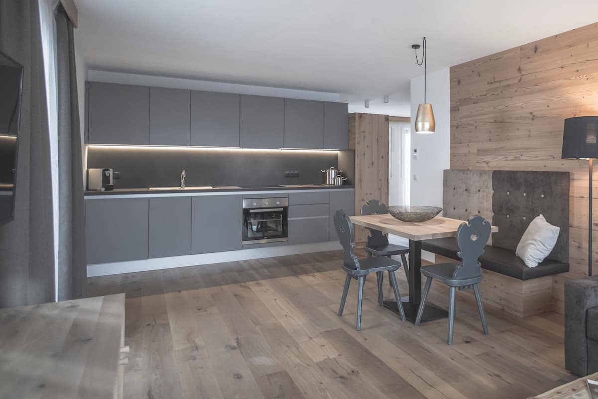 Cozinha moderna com armários cinza, uma mesa de jantar de madeira e um forno embutido.