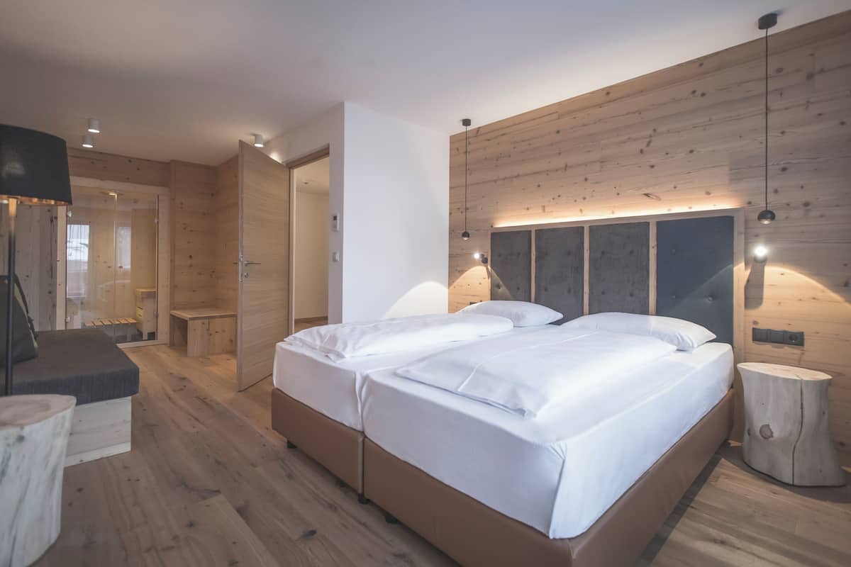 Quarto moderno com cabeceira de madeira, duas camas, abajures e piso de madeira.