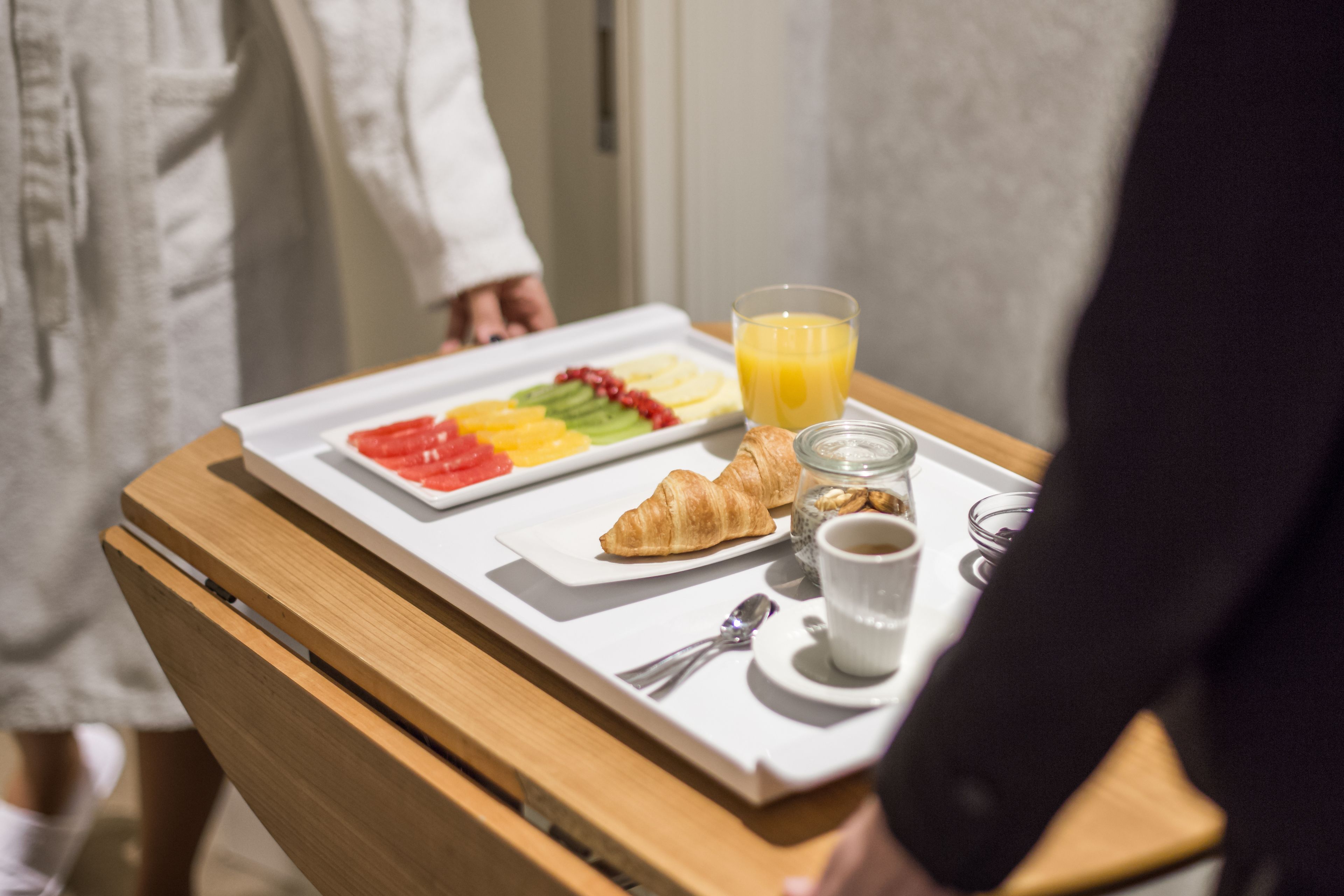 Bandeja de café da manhã com croissants, frutas e suco de laranja sobre uma mesa de madeira.