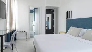 Quarto de hotel com uma cama grande, uma escrivaninha com cadeira, uma mesinha de cabeceira e uma TV fixada na parede.