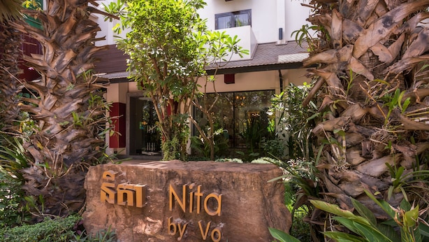 Uma placa de pedra com o nome 'Nita by Vo', rodeada por vegetação tropical exuberante e palmeiras.