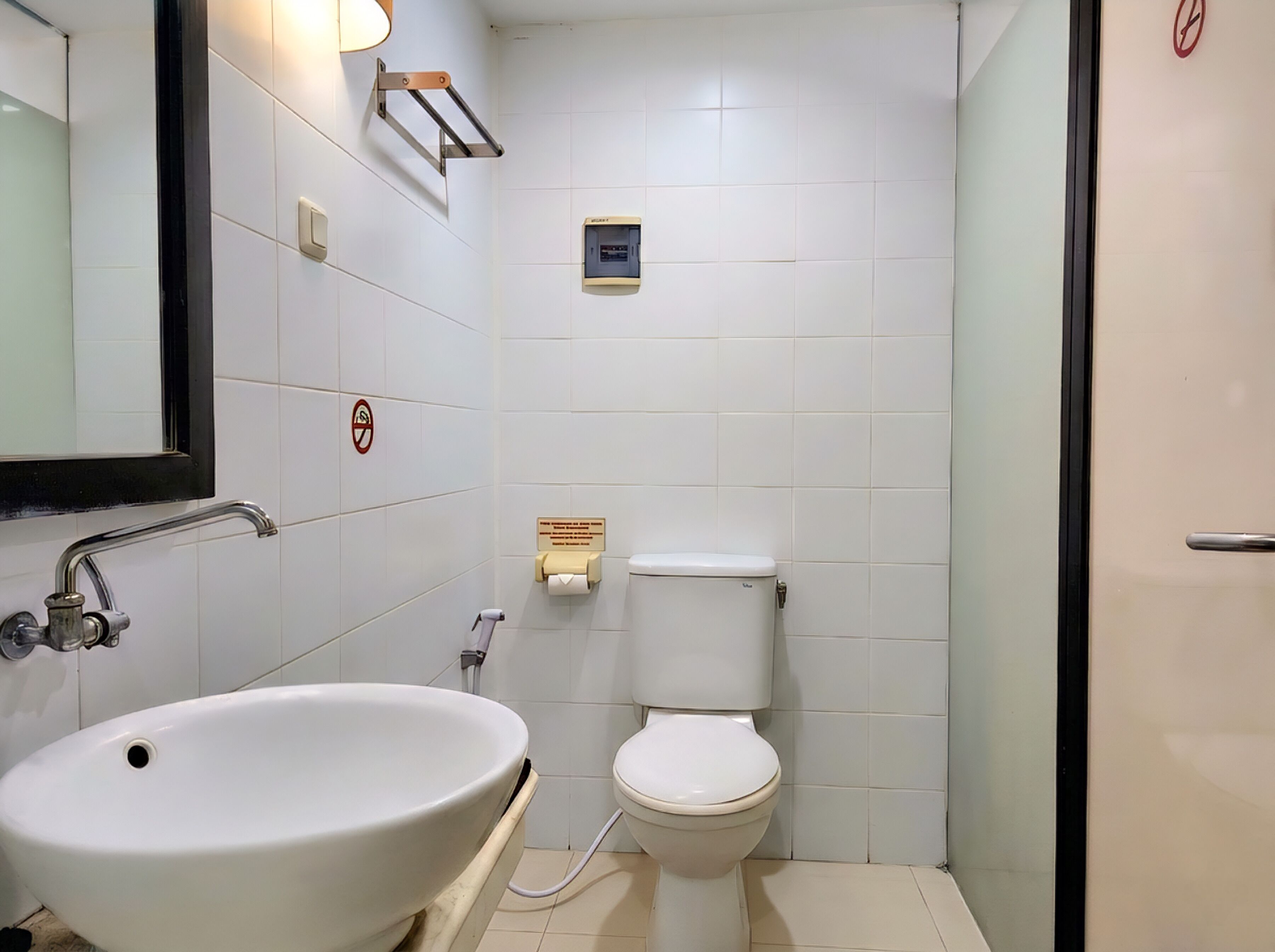 Casa de banho pequena e limpa, com lavatório branco, sanita e espelho.