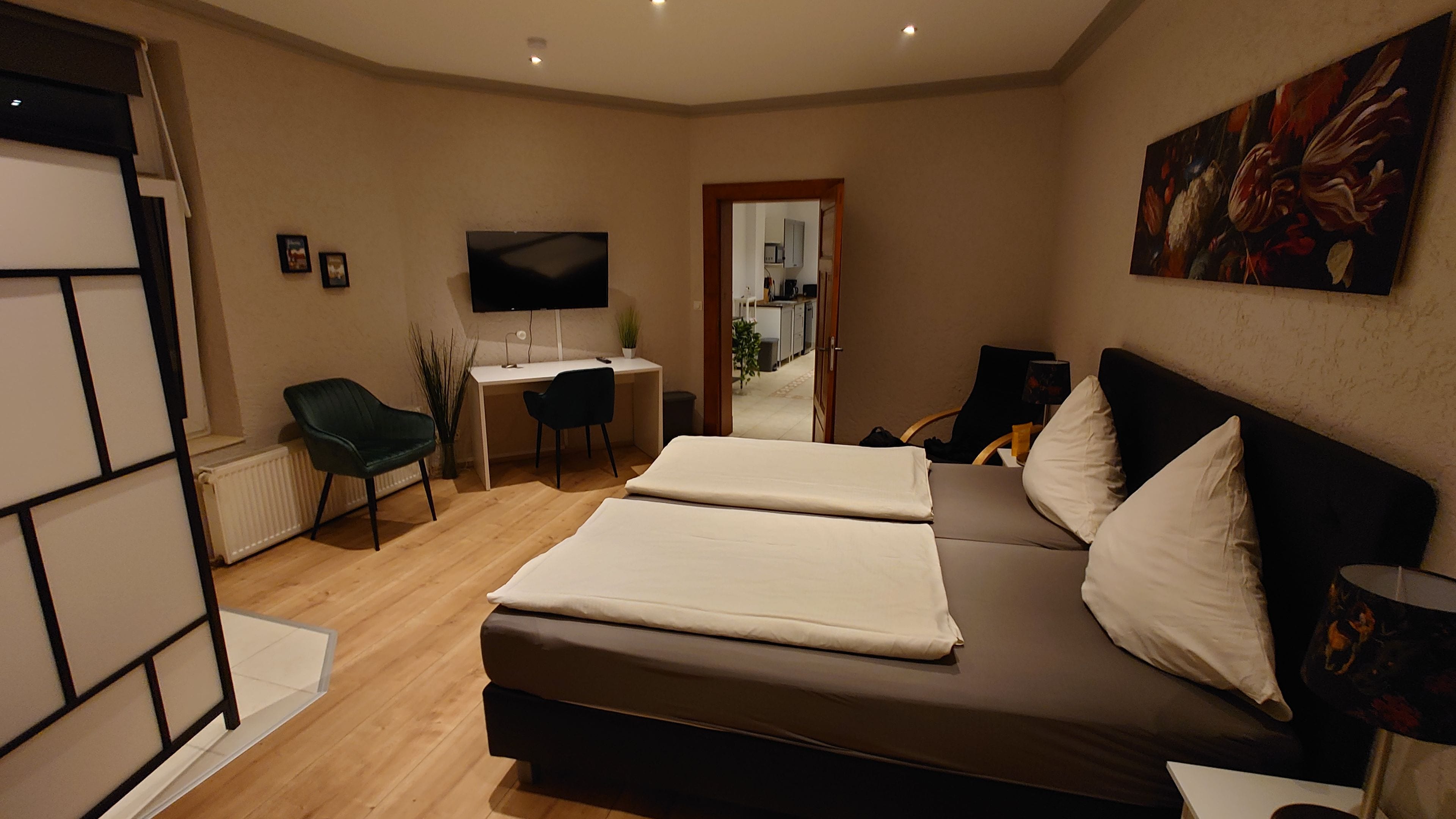 Quarto de hotel com cama, escrivaninha, cadeira, televisão e um quadro na parede.