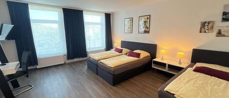 Quarto de hotel com duas camas, uma mesa, uma cadeira e uma janela com cortinas.