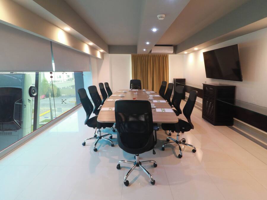 Sala de conferência com uma mesa comprida, cadeiras, uma TV e um muro de vidro.