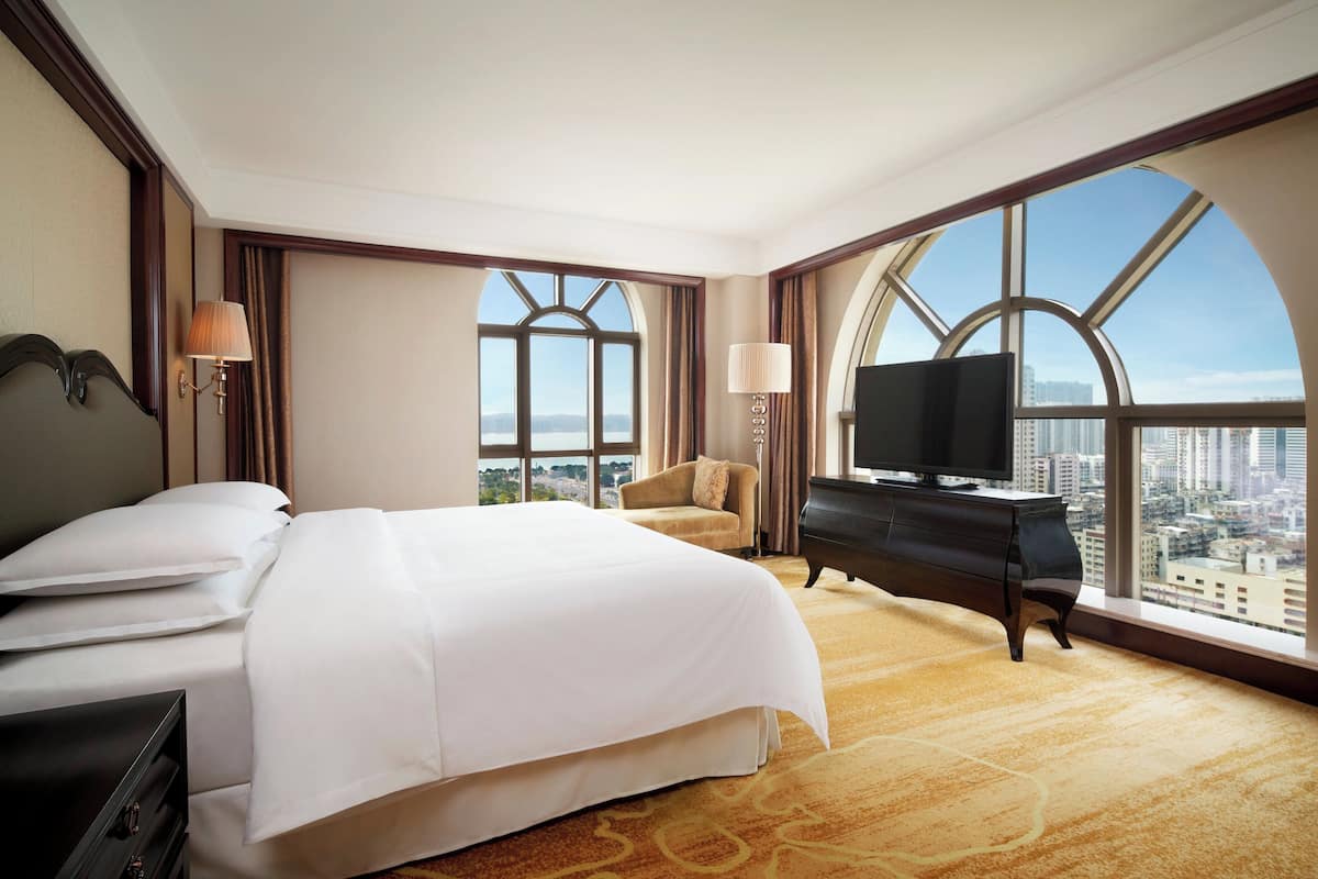 Quarto de hotel com uma cama grande, televisão, piano e vista da cidade.