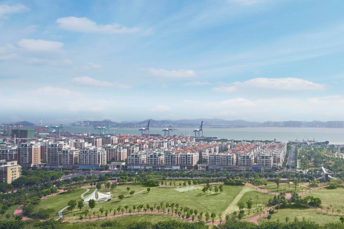 Um complexo de edifícios residenciais altos com vista para a orla marítima, áreas verdes e um amplo parque.