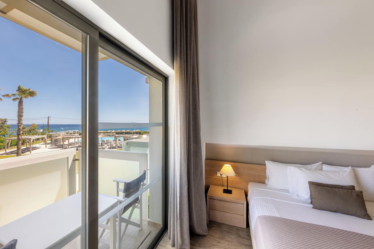 Quarto de hotel com uma janela grande que oferece vista para a piscina e palmeiras.