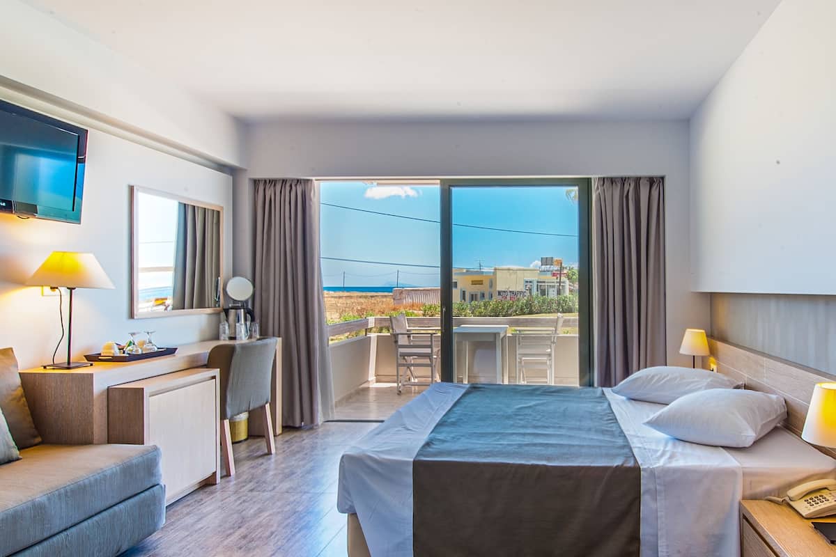 Quarto de hotel com cama, escrivaninha, cadeira, televisão e varanda com vista.