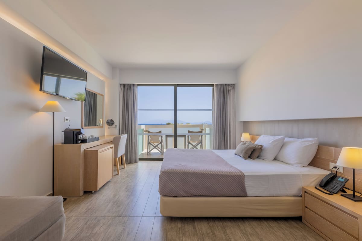 Quarto de hotel com cama, mesa de cabeceira, escrivaninha, cadeira e varanda com vista.
