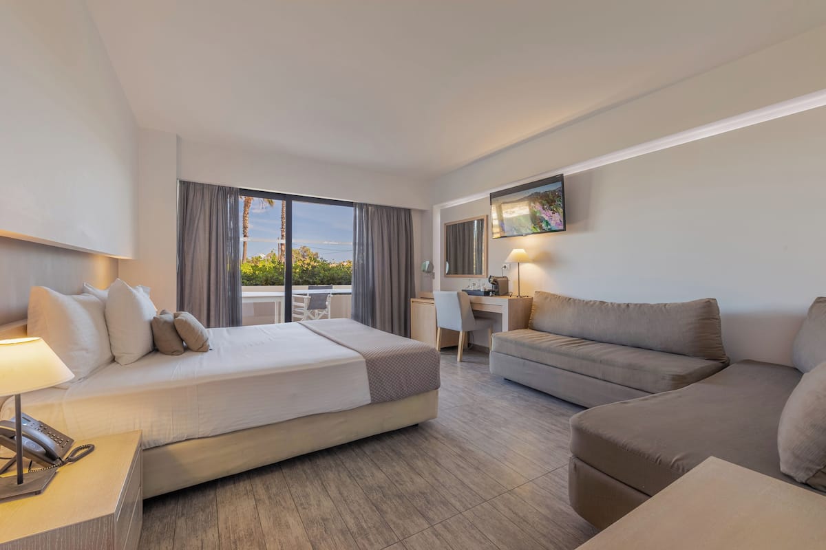 Quarto de hotel moderno com uma cama grande, um sofá, uma escrivaninha e uma varanda com vista.