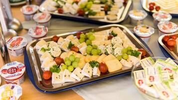 Uma mesa de buffet com vários queijos, uvas e pequenos recipientes de molhos.