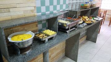 Uma mesa de buffet com diversos alimentos, incluindo arroz amarelo, ovos mexidos e pão.