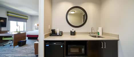 Quarto de hotel pequeno com cozinha compacta, uma cama, escrivaninha e televisão.