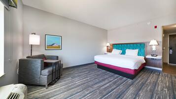 Quarto de hotel com cama, escrivaninha, cadeira, quadro na parede e porta.