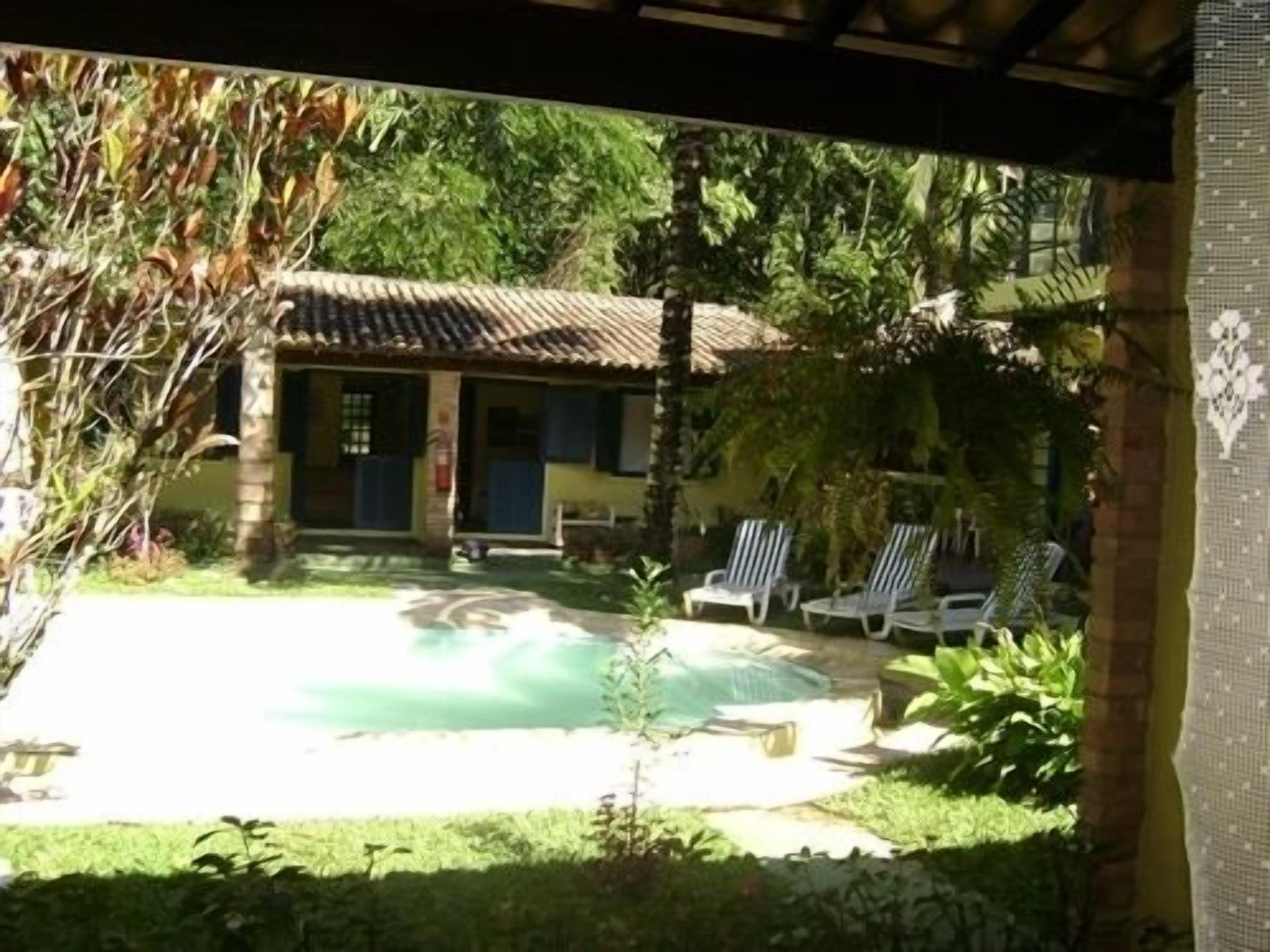 Uma área de piscina com espreguiçadeiras, um pequeno edifício e vegetação exuberante.