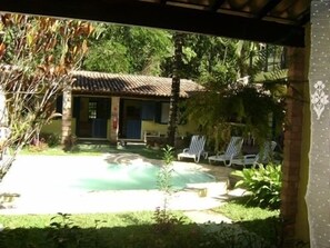 Uma área de piscina com espreguiçadeiras, um pequeno edifício e vegetação exuberante.