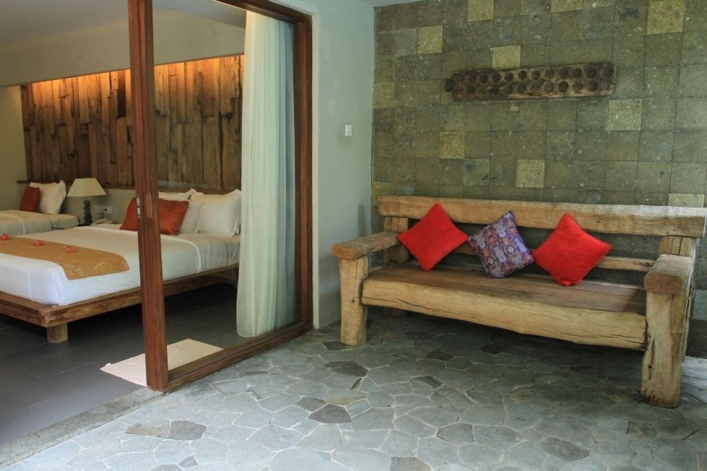 Um quarto com cama de madeira, um banco com almofadas e piso de ladrilho.