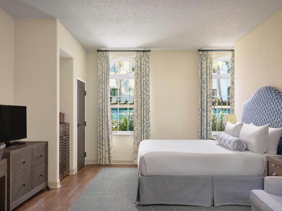 Quarto de hotel com uma cama, televisão, cômoda e janela com cortinas.