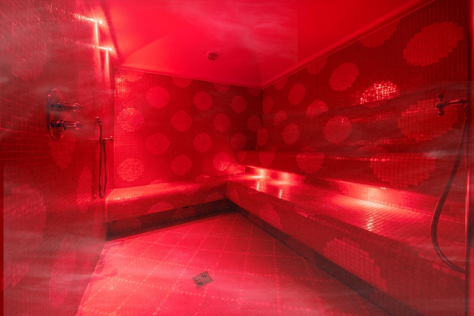 Quarto com iluminação vermelha, parede estampada, um banco e área de chuveiro.