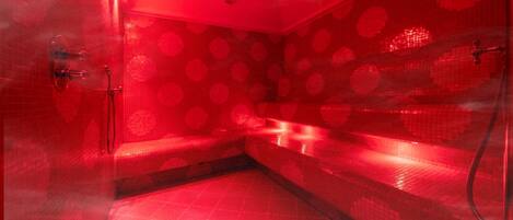 Quarto com iluminação vermelha, parede estampada, um banco e área de chuveiro.