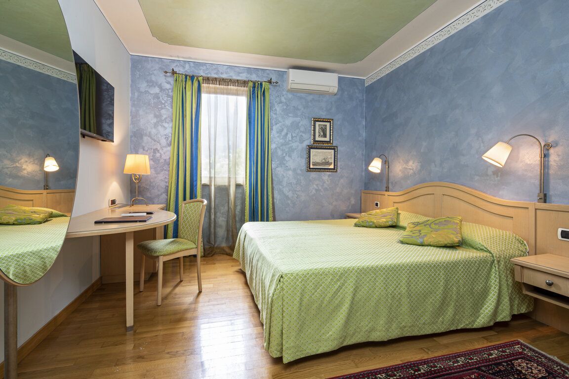 Quarto com cama, escrivaninha, cadeira e abajures de cabeceira.