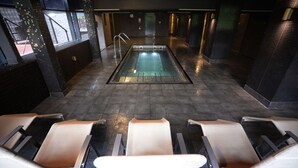 Uma área interna de piscina moderna com barreira de vidro, duas espreguiçadeiras e piso revestido de azulejos.