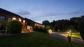 Hotel com fachada bem iluminada, calçada e jardim ajardinado.