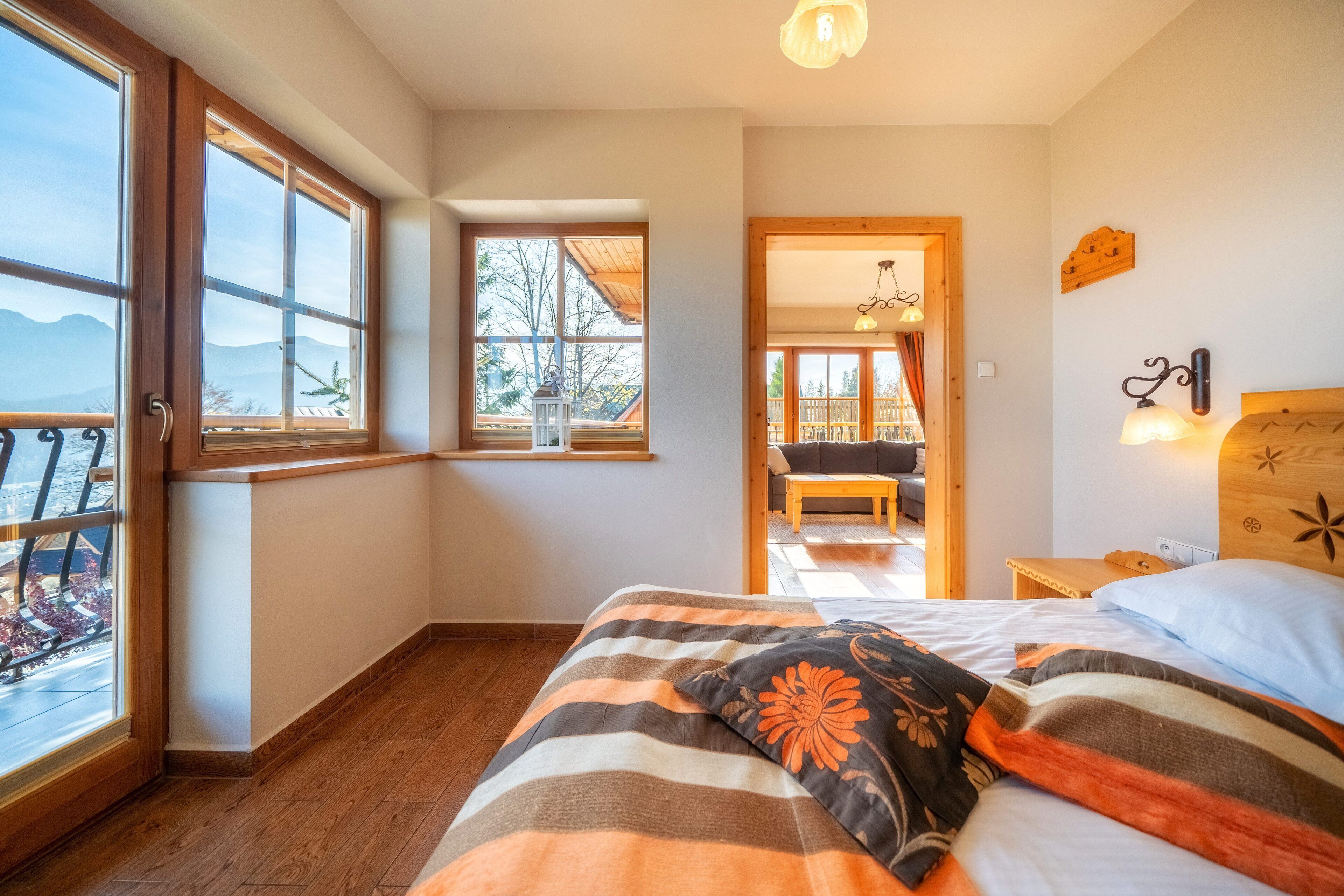 Quarto com uma janela grande, assoalho de madeira, cama com roupa de cama listrada e vista para montanhas.