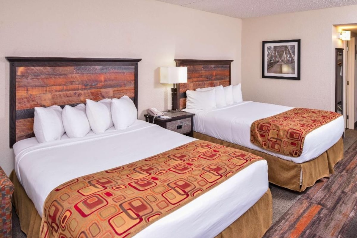 Quarto de hotel com duas camas, uma mesa de cabeceira, uma luminária e um quadro na parede.