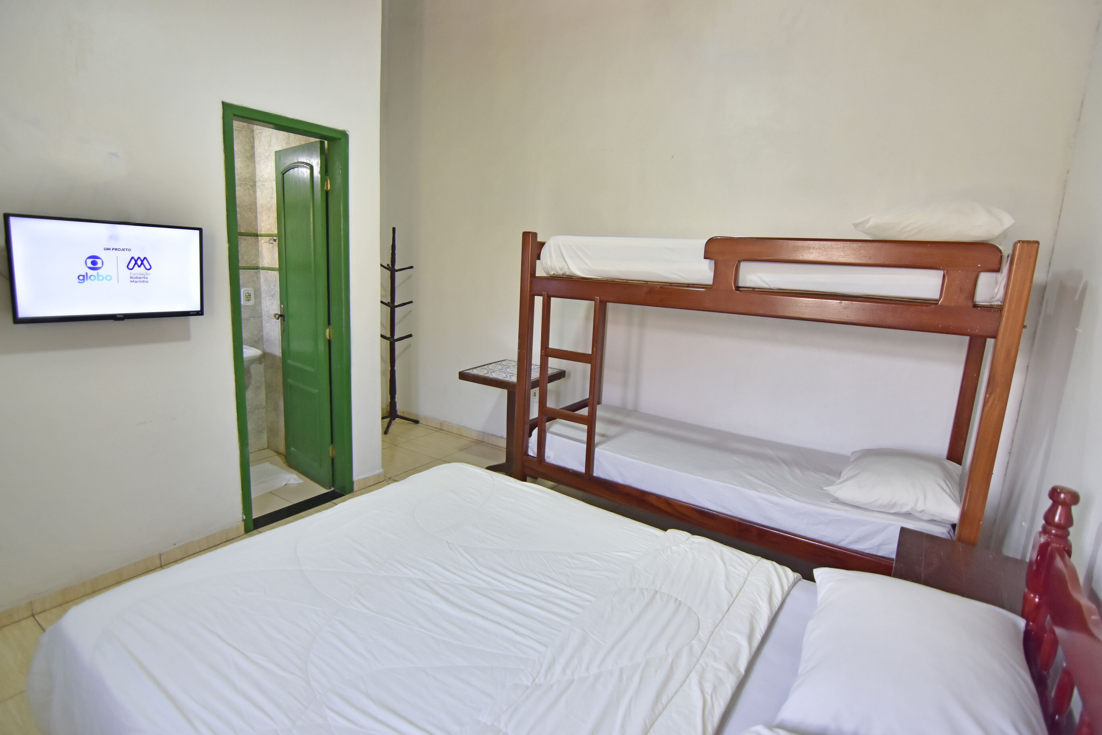 Um quarto com beliches, uma televisão na parede e uma porta verde.