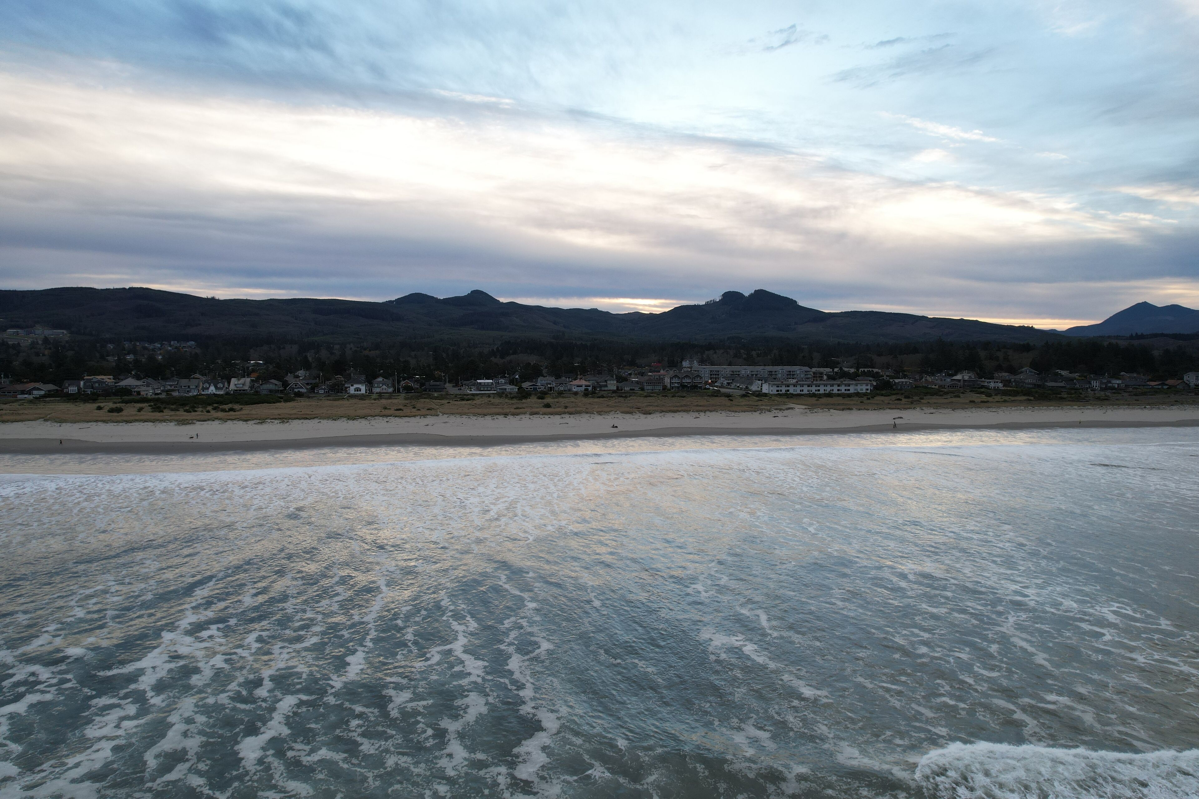 Paisagem costeira com praia, montanhas e uma cidade ao fundo.