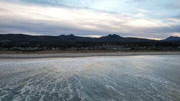 Paisagem costeira com praia, montanhas e uma cidade ao fundo.