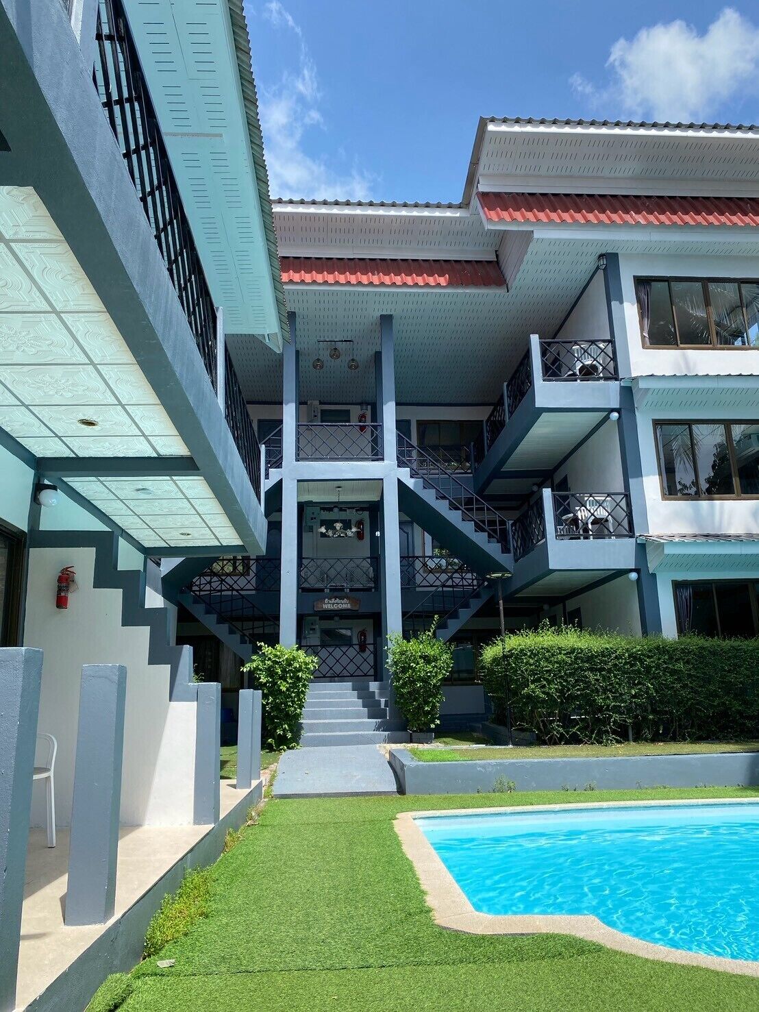 Um edifício com vários andares, piscina, escadaria e uma placa com a mensagem 'Bem-vindo'.