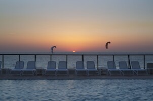 Vista do pôr do sol a partir de uma varanda com cadeiras de descanso voltadas para o mar.